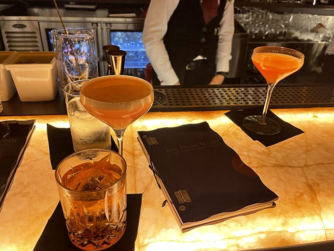 The signature smoked Old Fashioned arrives with theatrical flair, releasing aromatic wisps that enhance both flavor and the speakeasy experience.