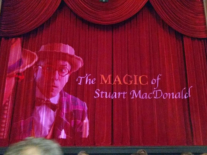 The stage curtain, emblazoned with "The MAGIC of Stuart MacDonald," promises an evening of wonder and illusion to come.