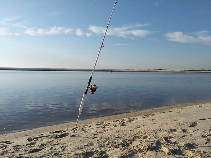 A fishing rod stands at attention against the horizon, patient sentinel for the day's catch while waves provide a soothing soundtrack.