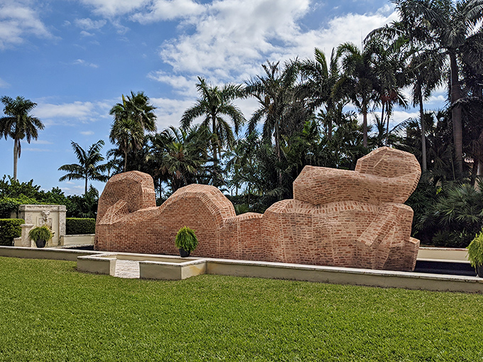 Massive brick sculptures rise like mountains from the earth, their imposing forms creating a dramatic contrast with the delicate palm fronds.