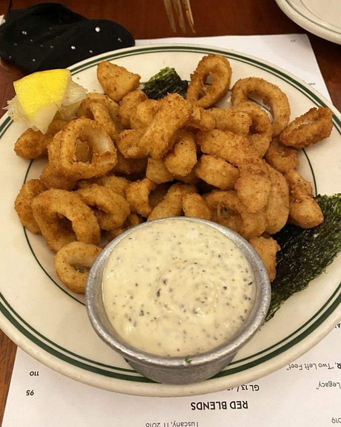 Golden-fried calamari achieves that elusive perfect texture &ndash; tender rings encased in a light, crispy coating, served with a creamy dipping sauce and lemon wedge.