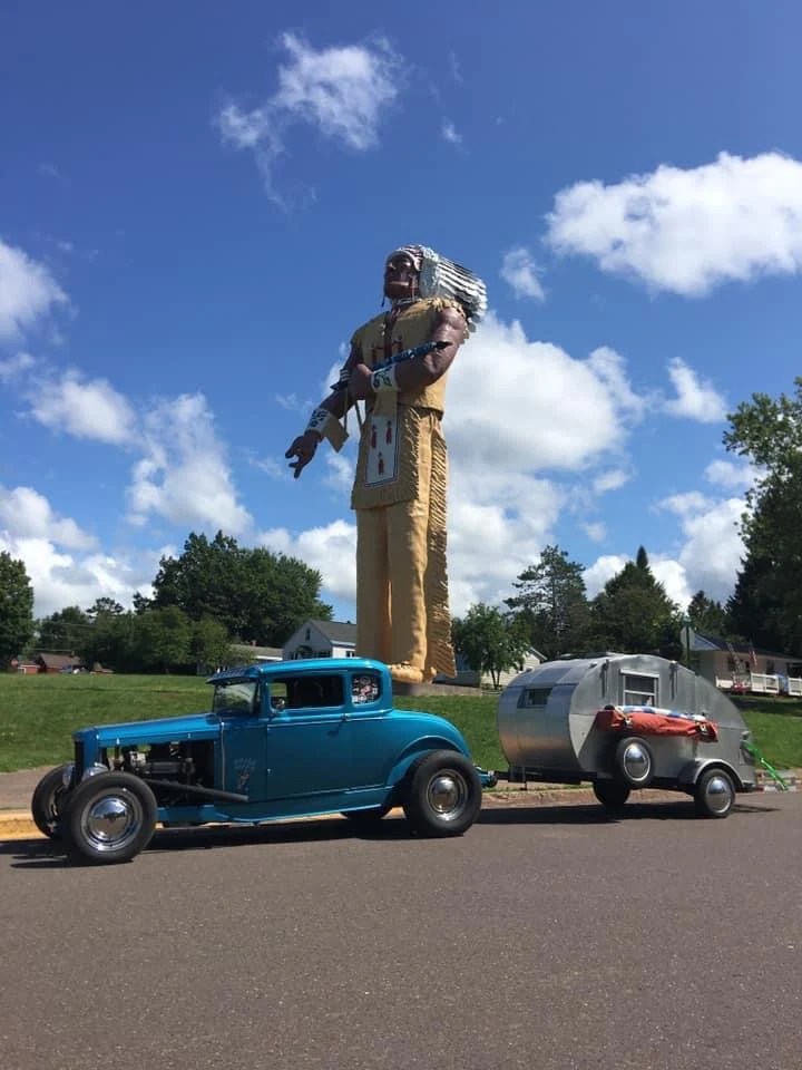 A classic hot rod and vintage trailer parked near Hiawatha create a perfect time-capsule scene that could have been lifted straight from a 1960s postcard.