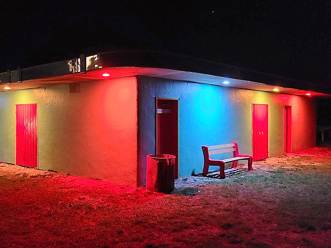 Night transforms the humble concession building into a neon-lit oasis of movie treats, red and blue lights guiding hungry patrons.