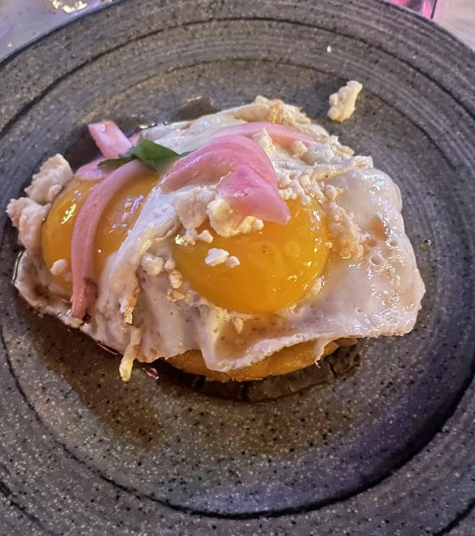 A sunny-side-up egg crowns this hearty breakfast creation, with pickled onions adding a pop of color and tang to cut through the richness.