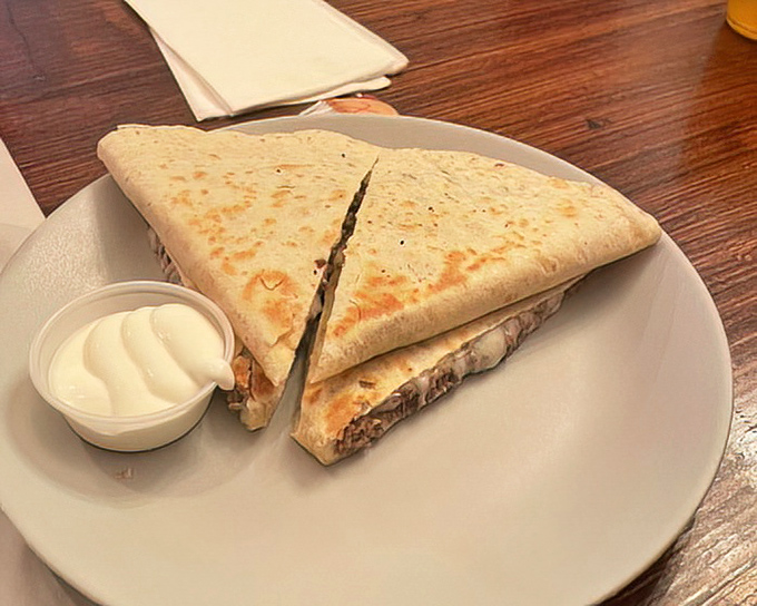 Perfectly grilled tortilla reveals a treasure of melted cheese and fillings, with that little cup of sour cream standing by for creamy reinforcement.