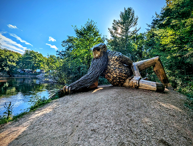 Benny the Beard Fisher reclines peacefully by the Fox River, his massive wooden form blending harmoniously with the Michigan wilderness.