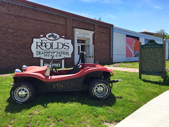 The brick facade of R.E. Olds Transportation Museum welcomes visitors with a vintage dune buggy parked out front, hinting at the treasures inside.