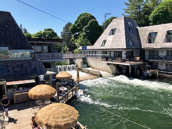 The Cove's distinctive A-frame buildings straddle the rushing Leland River, where thatched umbrellas and waterfront decks create Michigan's most dramatic dining backdrop.