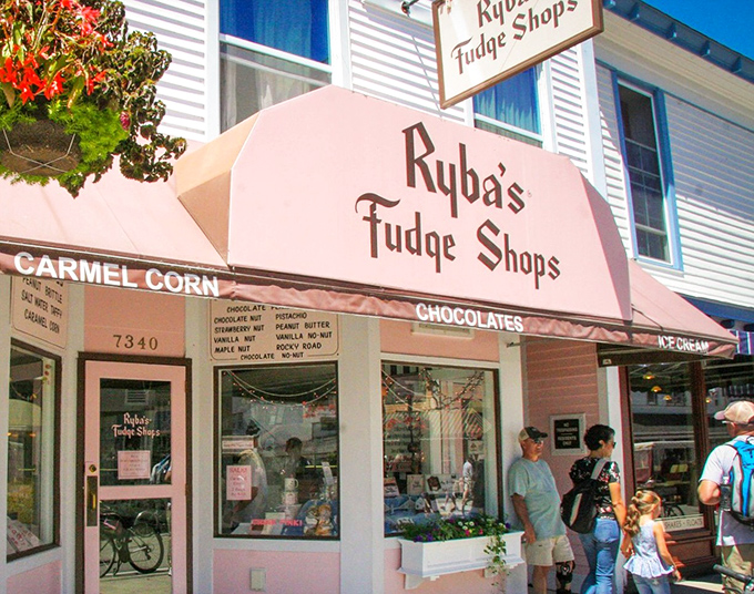 The iconic pink awning of Ryba's Fudge Shops stands as a sweet beacon on Mackinac Island's Main Street, promising sugary treasures within.