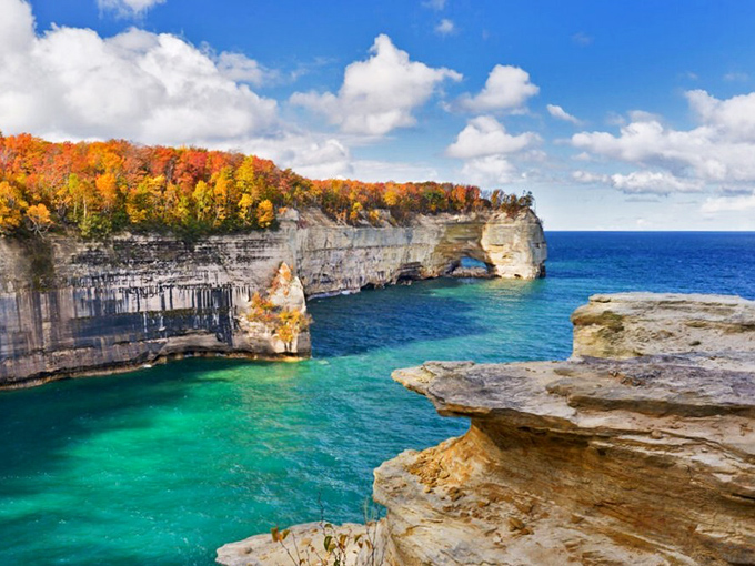Grand Portal Point stands like nature's masterpiece, where autumn fire meets Caribbean blue in a scene that defies Michigan stereotypes.