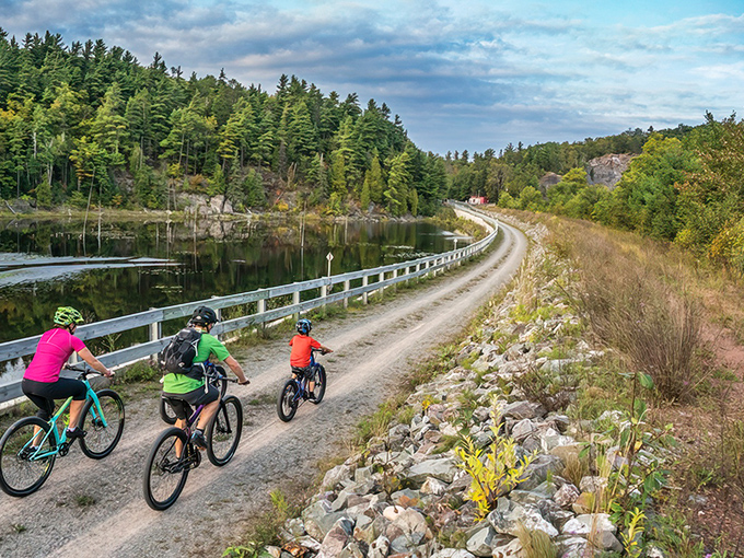 Three cyclists glide along the Iron Ore Heritage Trail, where pristine waters mirror towering pines &ndash; nature's own infinity pool with pedal power.