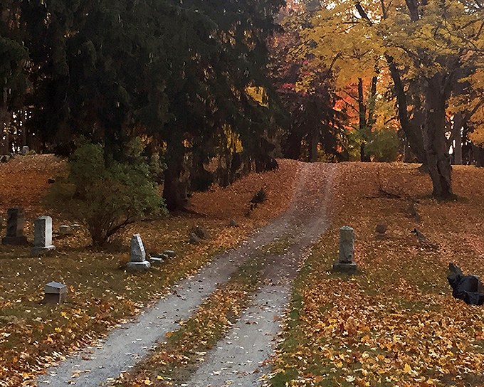 A winding path through autumn-kissed trees leads visitors deeper into Nunica Cemetery, where fallen leaves whisper secrets of those who rest beneath them.