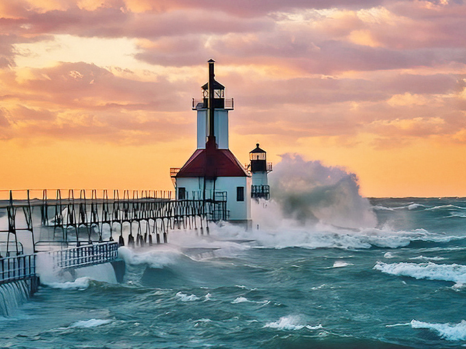 Sunset paints the St. Joseph lighthouse in fiery hues as waves crash dramatically against the pier &ndash; nature's most spectacular light show.