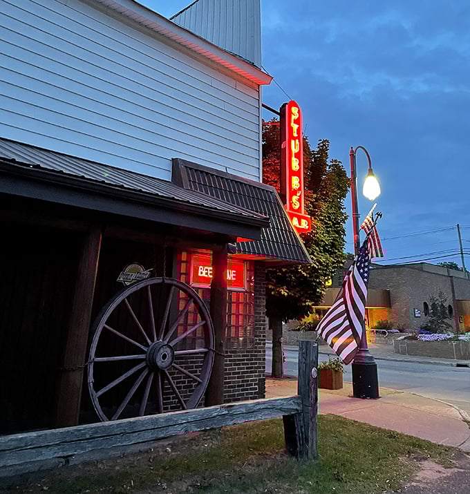 The iconic red neon "STUBBS BAR" sign glows against the twilight sky, beckoning curious travelers with promises of cold drinks and warm oddities.