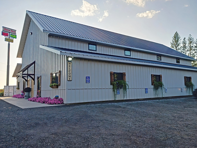 The charming barn-style exterior of Sweetly Kismet welcomes candy lovers with its clean white siding and vibrant pink flowers – a sweet prelude to the treasures inside.