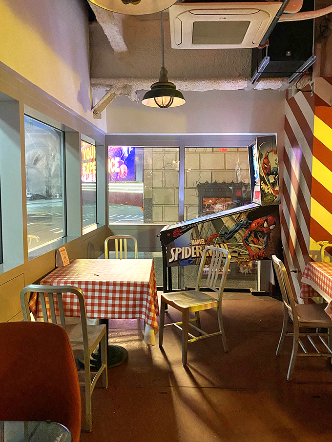 The intimate dining area features bold red and white stripes, industrial lighting, and that beloved pinball machine waiting for between-bite gaming sessions.