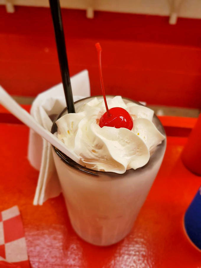This hot fudge malt isn't just dessert; it's therapy in a glass, topped with whipped cream and a cherry that's basically wearing a tiny dessert crown.