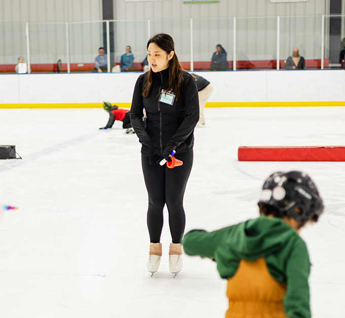 A skating instructor guides young learners through basic techniques, patience and encouragement evident in her stance.