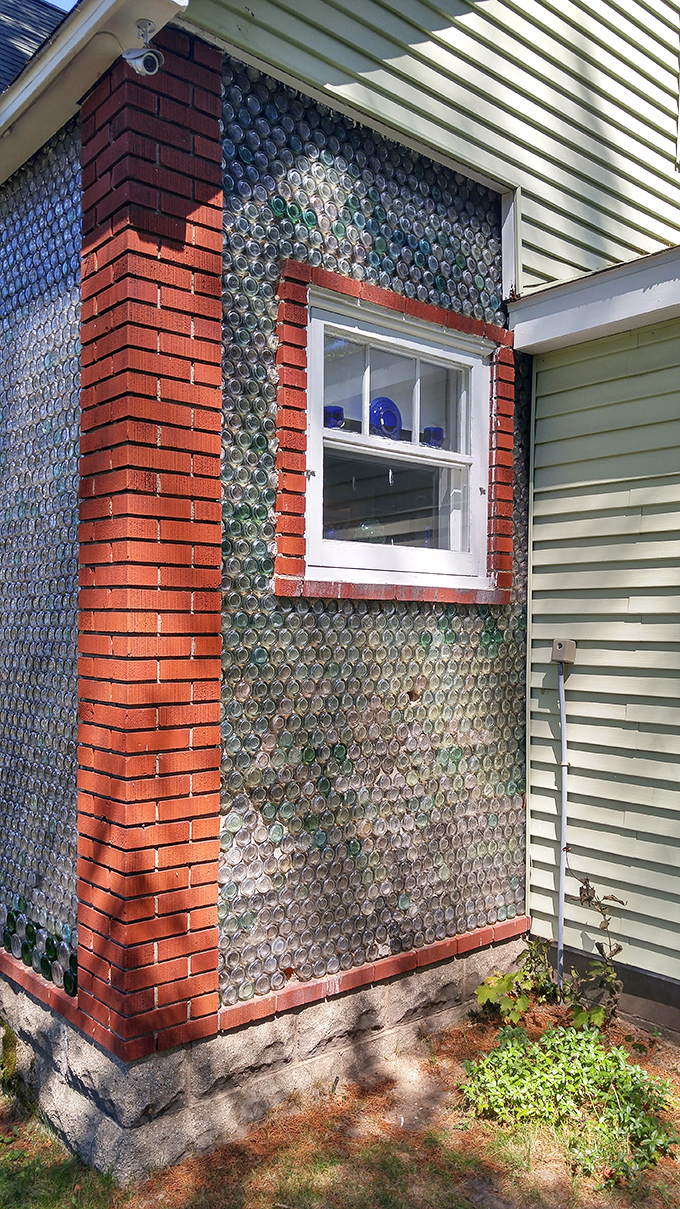 The window framed by bottle-embedded walls creates a striking contrast between conventional construction and the builder's innovative vision for using discarded materials.