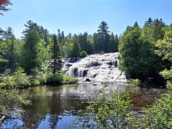 Sunlight dapples the impressive waterfall as it thunders into the clear pool below, creating a mesmerizing natural spectacle.