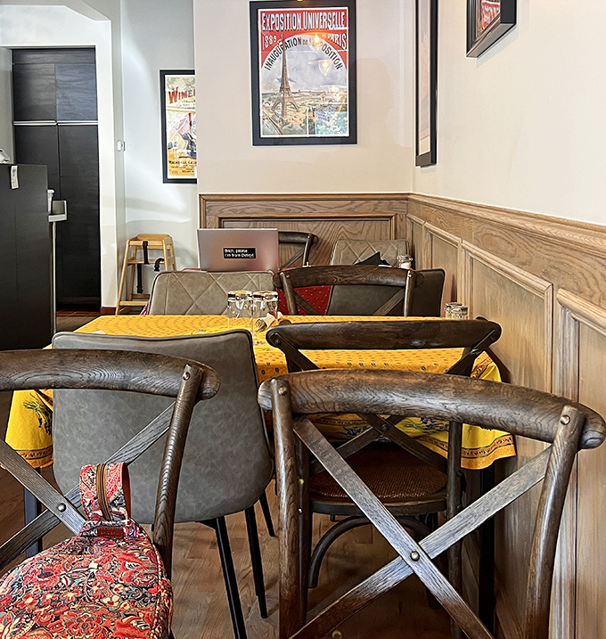 Wooden wainscoting and vintage French posters create an intimate dining space where conversations flow as easily as the coffee.