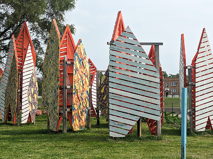 Wooden sail-like structures rise from the earth in the outdoor installation area, their bright patterns creating a surreal forest of color against the urban landscape.