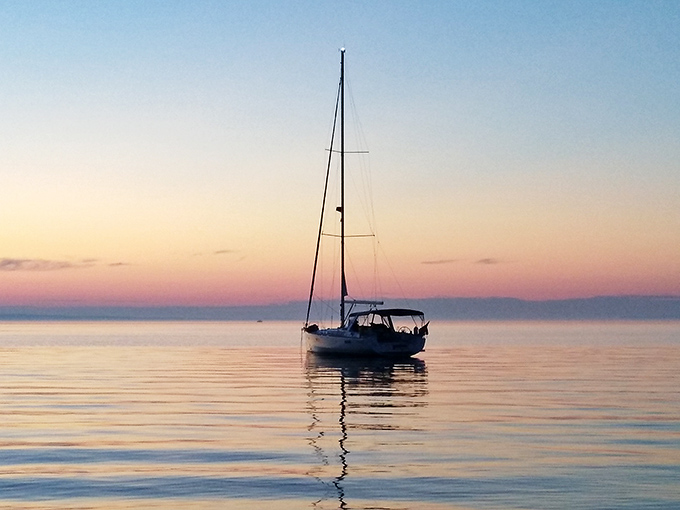 Solitary sailboat at dusk: where the boundary between water and sky dissolves into watercolor perfection.