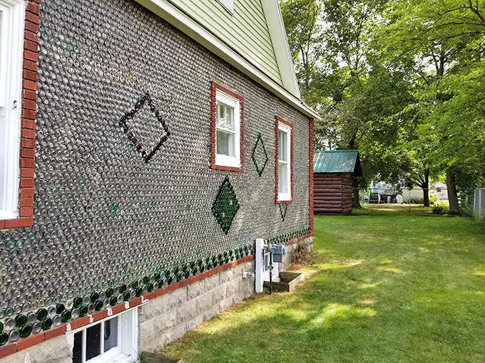 The side view reveals the extensive bottle work covering nearly every exterior surface, with green bottles creating decorative diamond patterns against clear glass backgrounds.