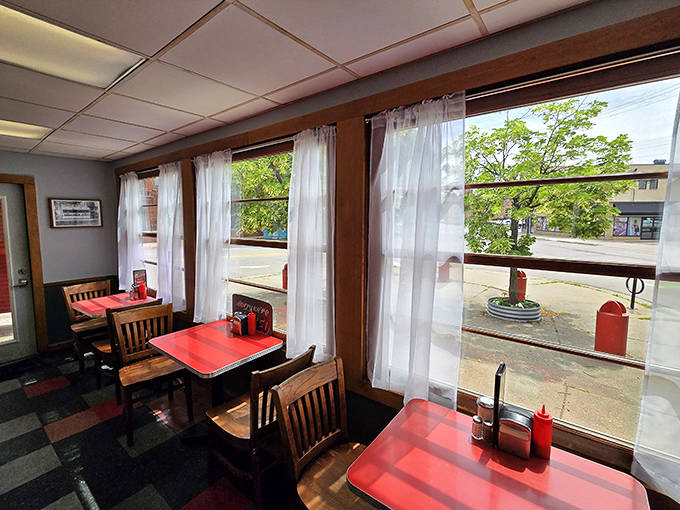 Sunlight streams through windows framed by simple curtains, illuminating red tables where generations have gathered to break bread and share stories.