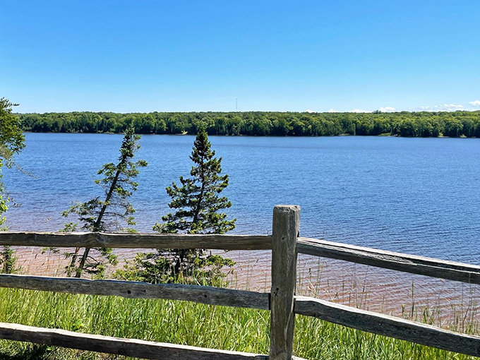Weathered fence posts stand sentinel over calm waters, framing nature's masterpiece in rustic simplicity.