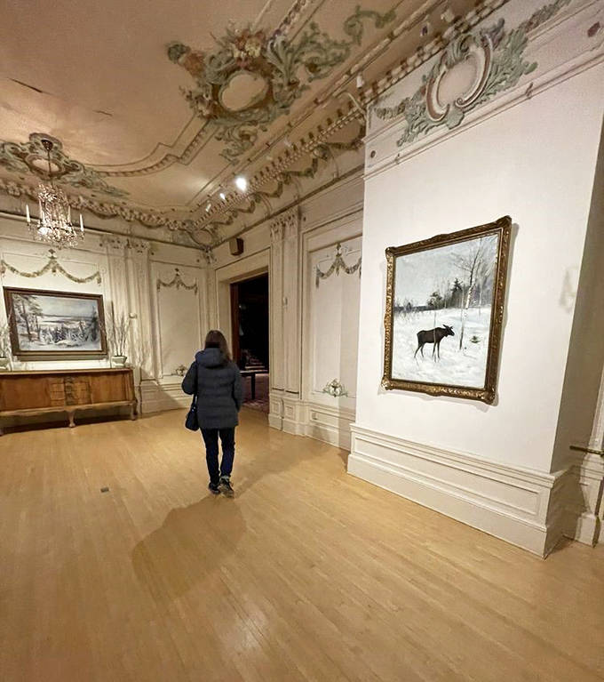 Visitors explore galleries where artwork hangs against pristine walls, the moose painting offering a quintessentially Nordic wilderness scene.