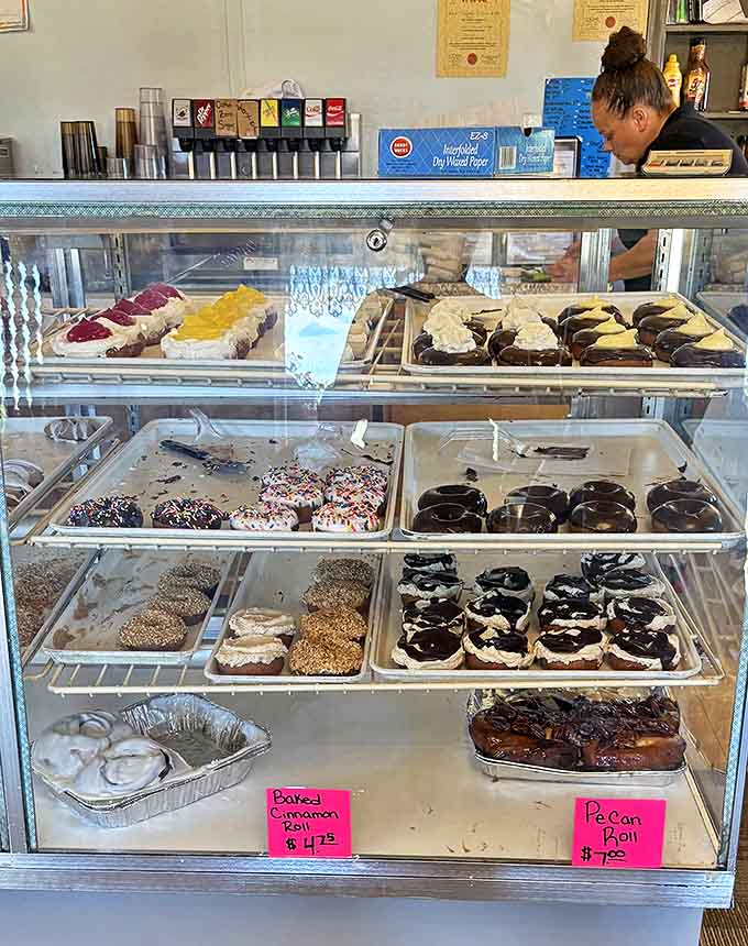 The display case of dreams – each shelf offering oversized pastry perfection that makes choosing just one nearly impossible.