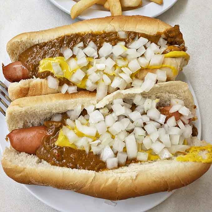 Two Coney dogs in their full glory &ndash; the snap of the natural casing, the savory chili, the sharp bite of onions, and that essential streak of mustard.