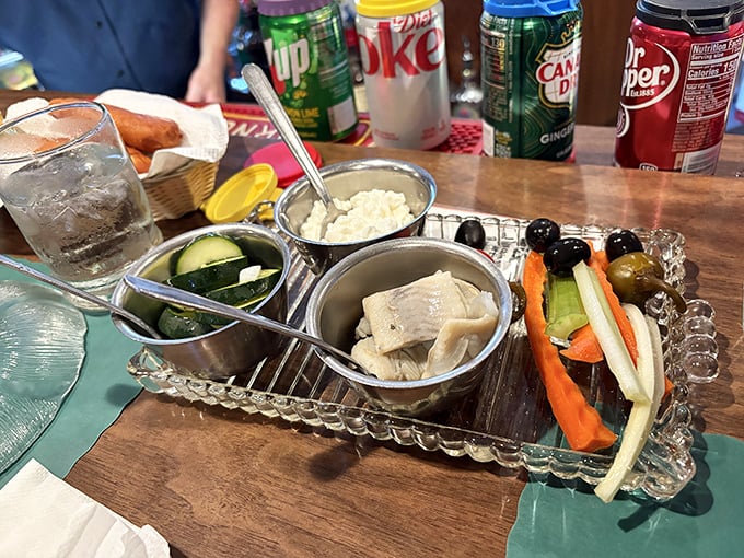 The relish tray arrives like an old friend – crystal-clear compartments holding crisp vegetables and pickles in a nostalgic presentation.