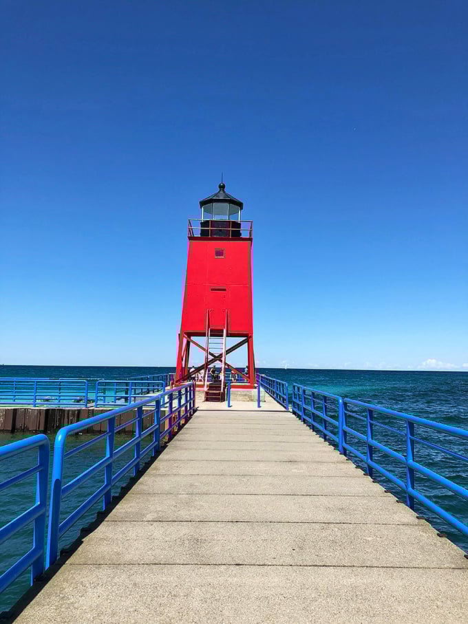 Standing tall against azure skies, this crimson lighthouse guides visitors to shores where Great Lakes adventures begin.