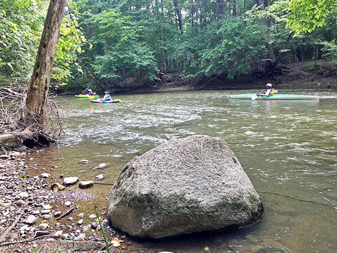 Kayakers navigate gentle waters past a boulder that's been perfecting its stoic pose since the last ice age.