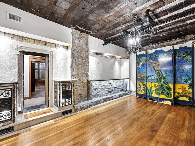 Exposed stone walls and wooden beams reveal the mansion's bones, while colorful artwork adds unexpected contemporary flair to this transitional space.