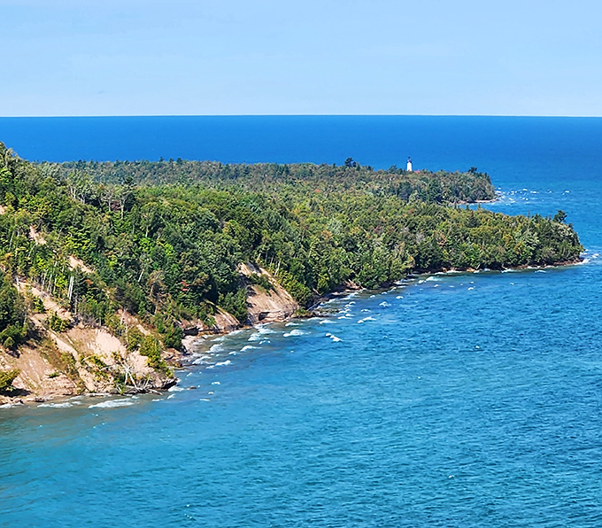 Forested peninsulas reach into Superior's azure waters, with the iconic lighthouse standing proud against the horizon.