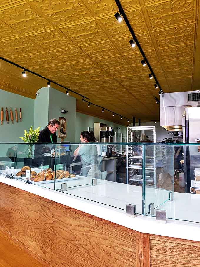 The open bakery layout invites customers to witness the craft behind their morning croissant. That gold ceiling adds unexpected luxury to this humble bread temple.