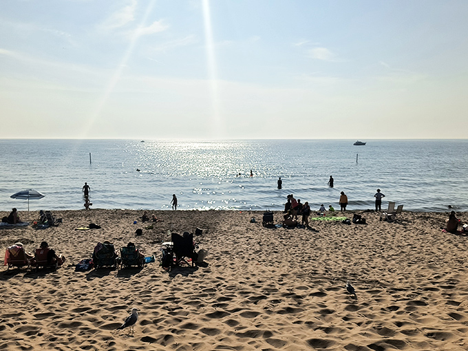 Beachgoers dot the shoreline like human sprinkles on a sandy sundae, each finding their perfect spot along Lake Michigan.