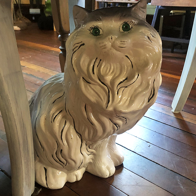 This ceramic cat with emerald eyes seems to be judging your life choices from its perch on the hardwood floor.