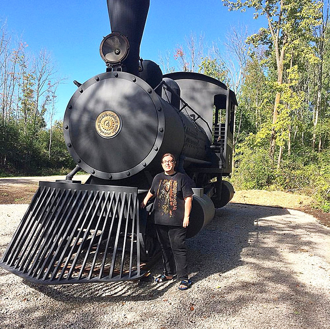 This train enthusiast found his happy place beside the vintage locomotive, probably contemplating how many steering wheels it once transported in its heyday.