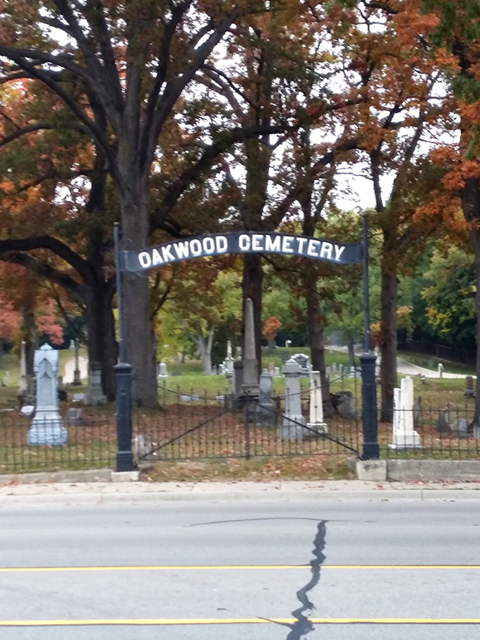 The cemetery's name arches gracefully above the entrance, framed by autumn foliage that adds seasonal drama to this historic site.