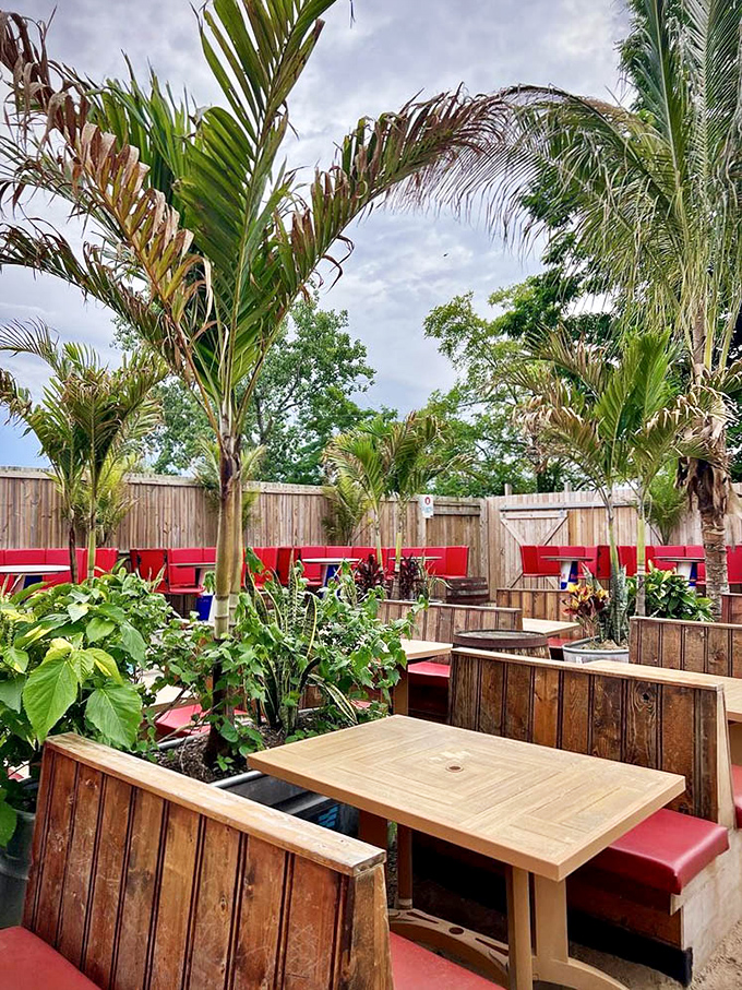 Outdoor seating areas blend natural wood with bright red accents, creating intimate conversation spaces beneath swaying palm fronds.