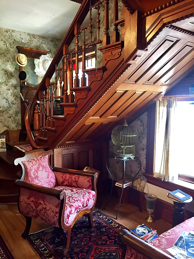 Sitting Area: The grand staircase curves gracefully above plush red chairs, creating a cozy nook where Victorian elegance meets modern comfort.