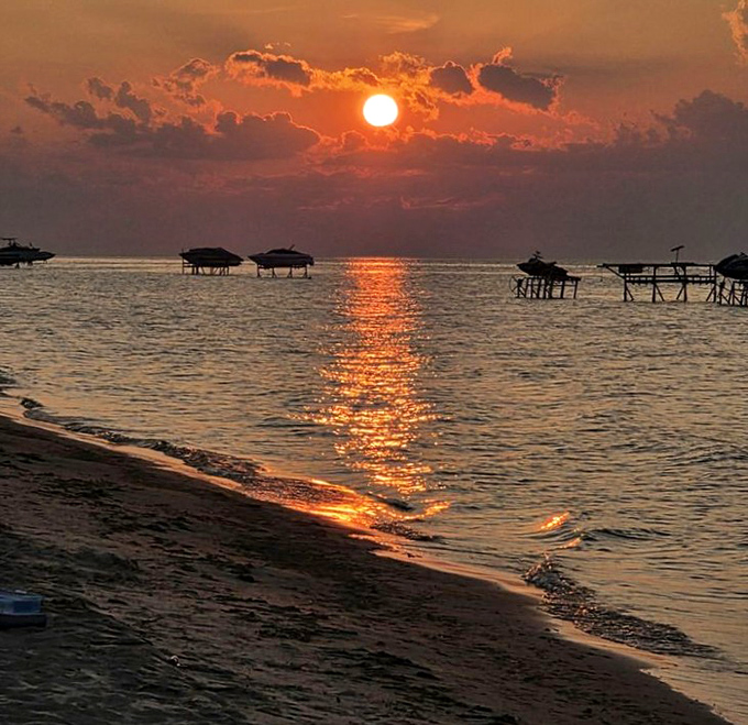 Sunset paints the water in impossible colors as boat lifts stand sentinel along the shoreline.