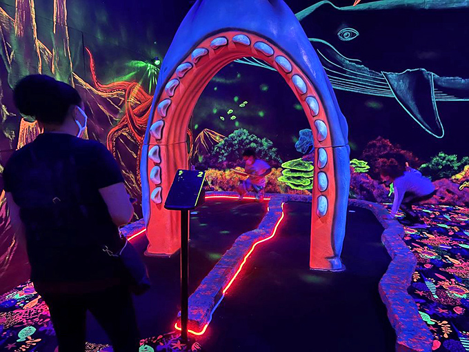 A visitor contemplates their next move beneath the glowing tentacles of a neon sea creature&mdash;mini-golf strategy has never been so atmospheric.