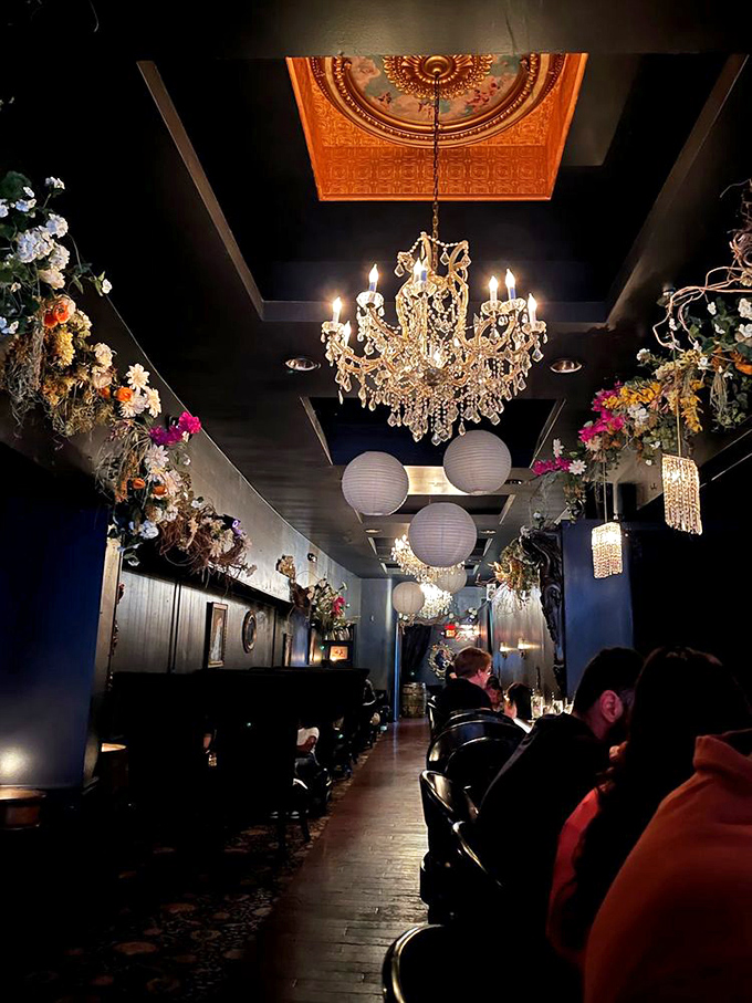 The ceiling blooms with dried flowers and paper lanterns, creating a magical garden effect that softens the dark sophistication of the walls and furnishings.