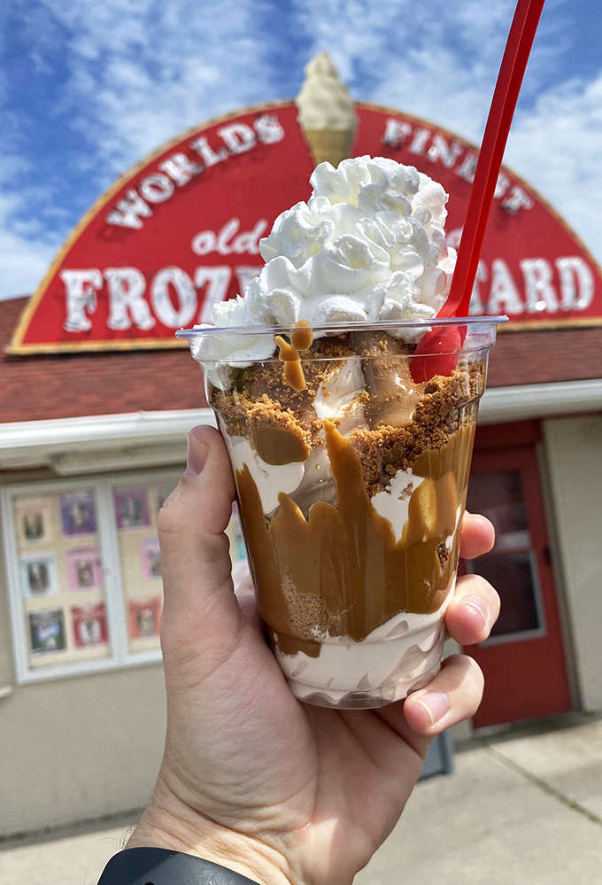 A caramel-drizzled masterpiece held against the iconic red sign &ndash; visual proof that sometimes the best souvenirs are edible.