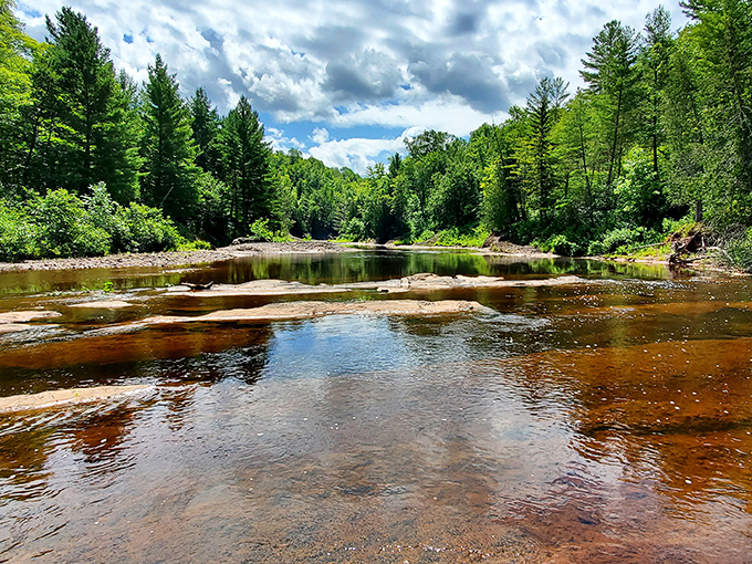 Summer serenity downstream: After the dramatic plunge, the river returns to a peaceful flow, inviting contemplation among the sun-dappled stones.